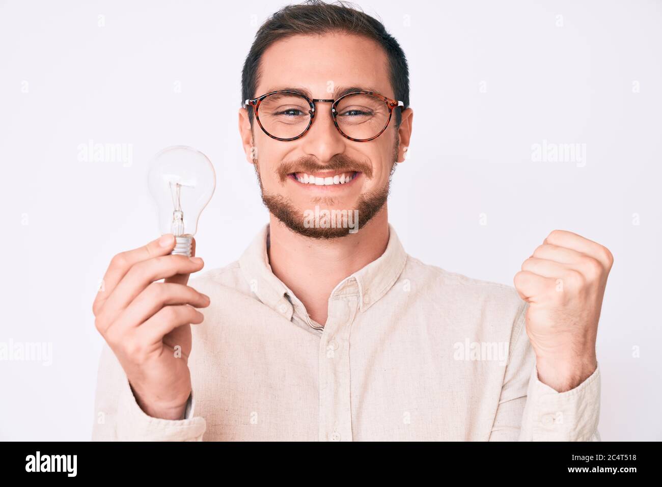 Young handsome man holding lightbulb for inspiration and idea screaming ...