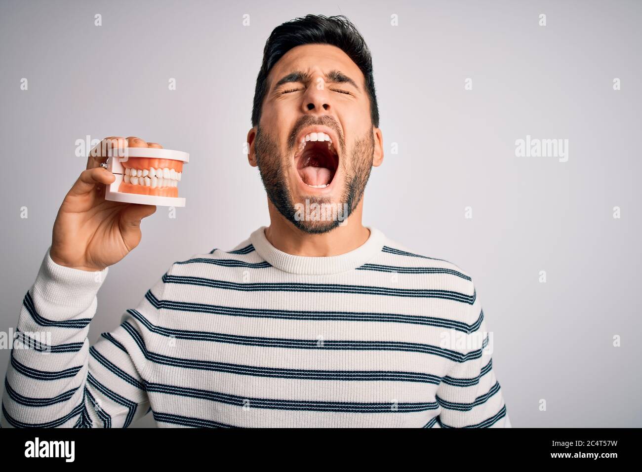 Young handsome man with beard holding plastic denture teeth over white ...