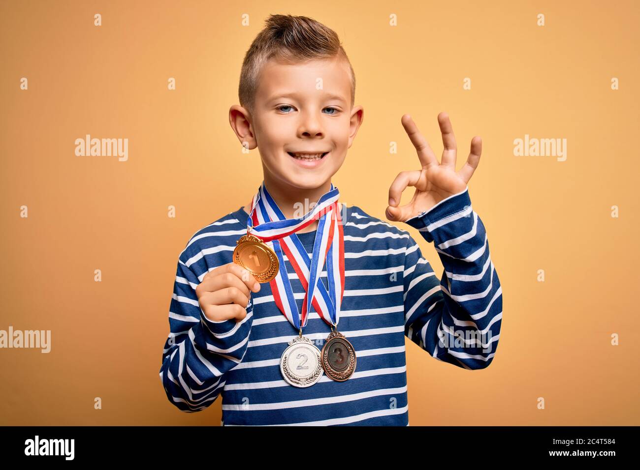 Young little caucasian winner kid wearing award competition medals over ...