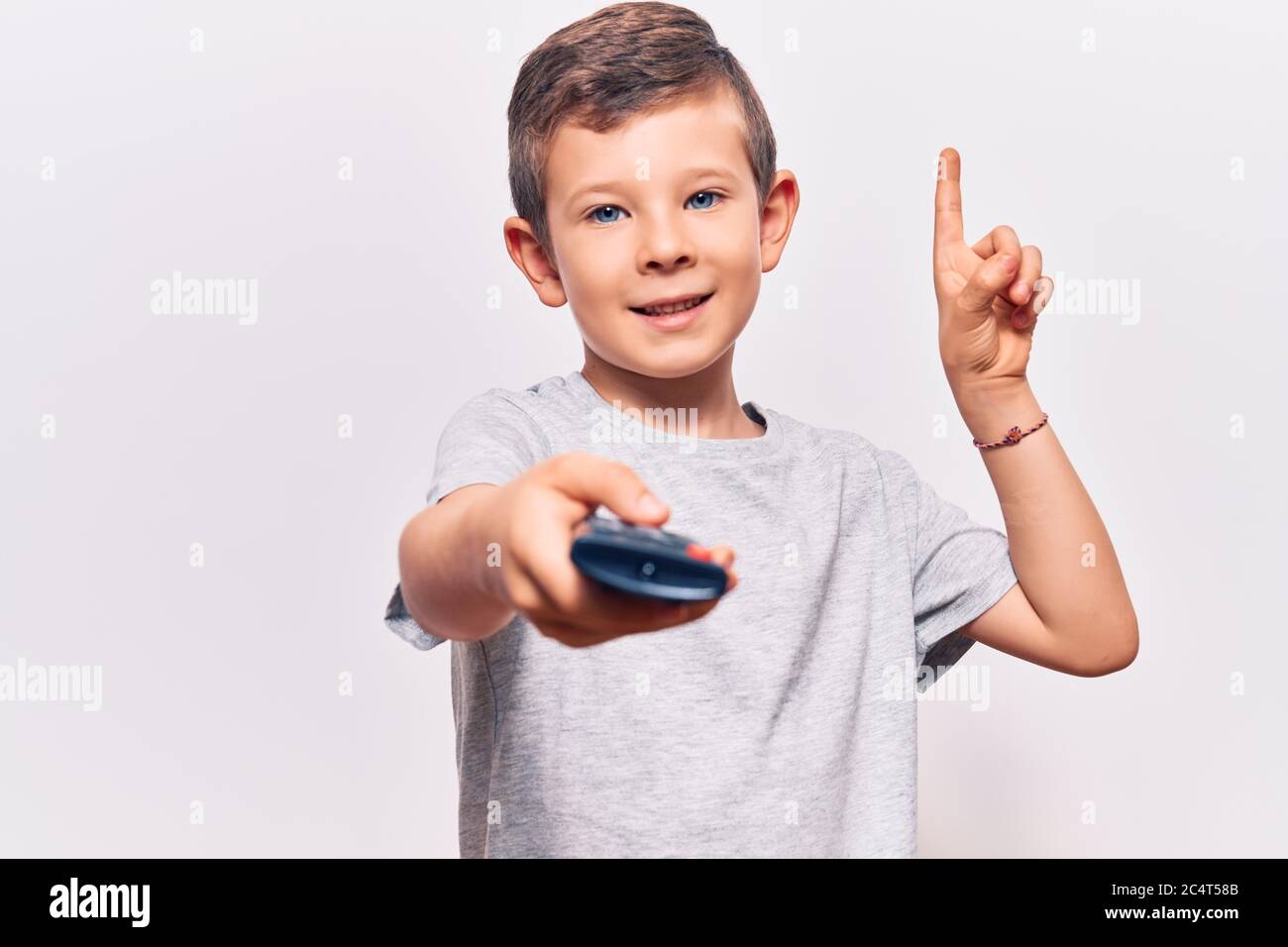 Cute blond kid holding television remote control smiling with an idea ...