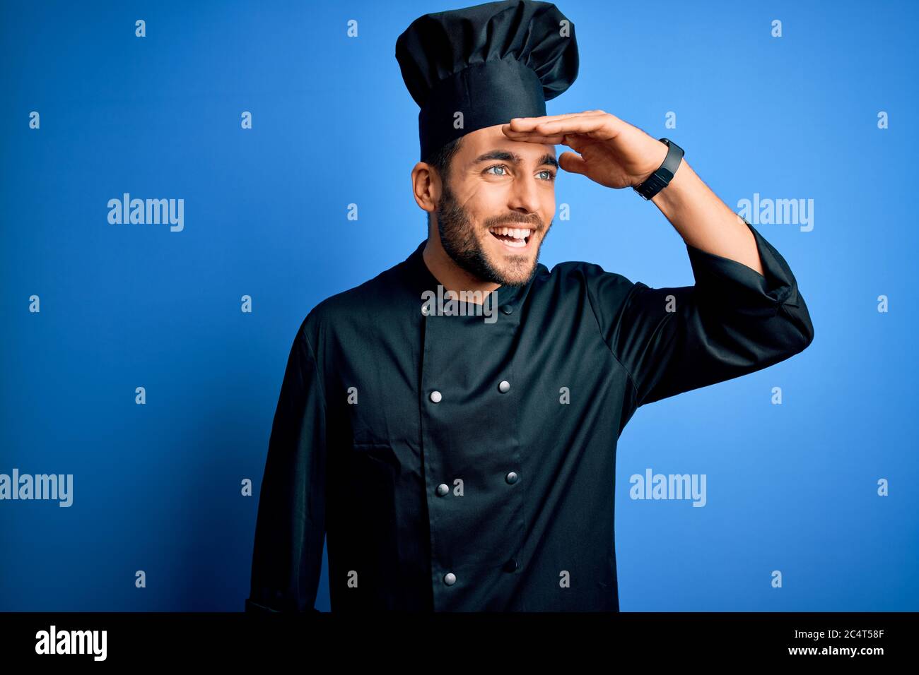 Young handsome chef man with beard wearing cooker uniform and hat over ...