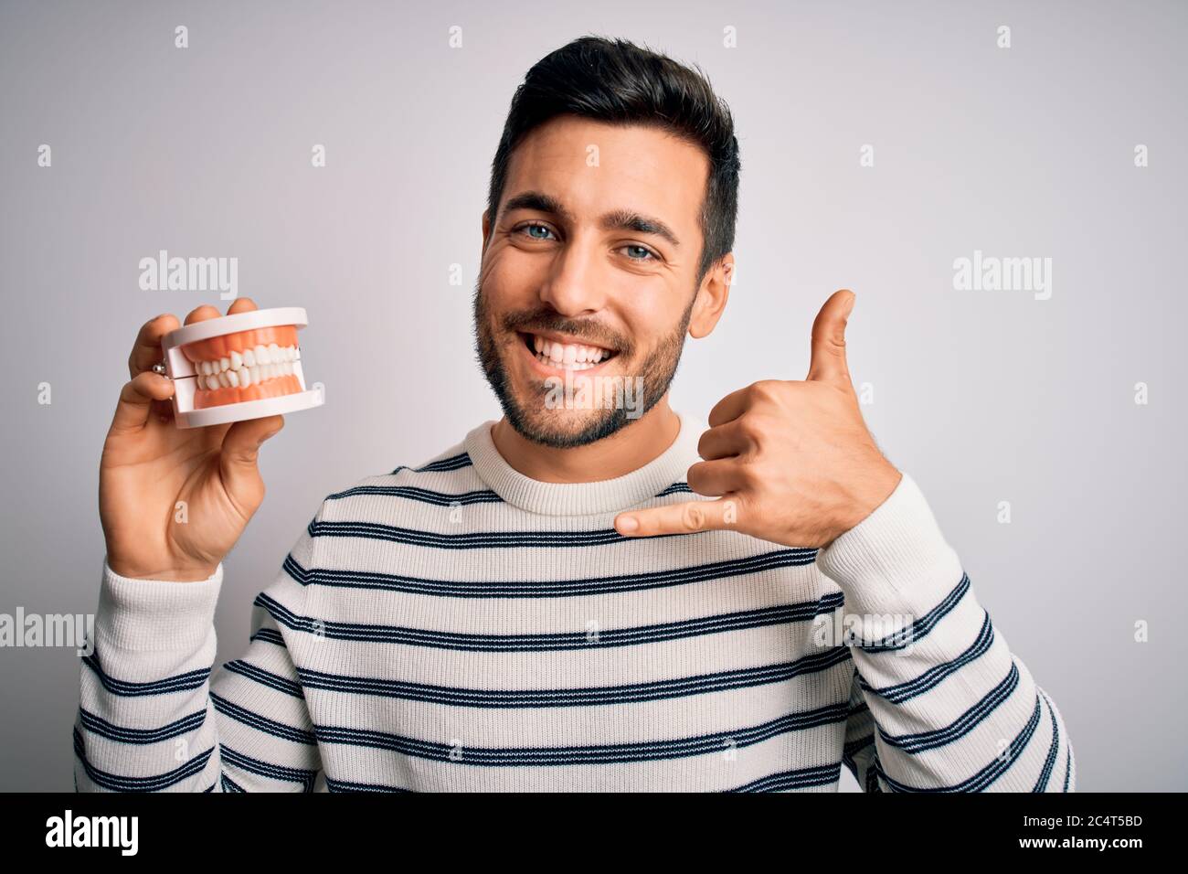 Young handsome man with beard holding plastic denture teeth over white ...