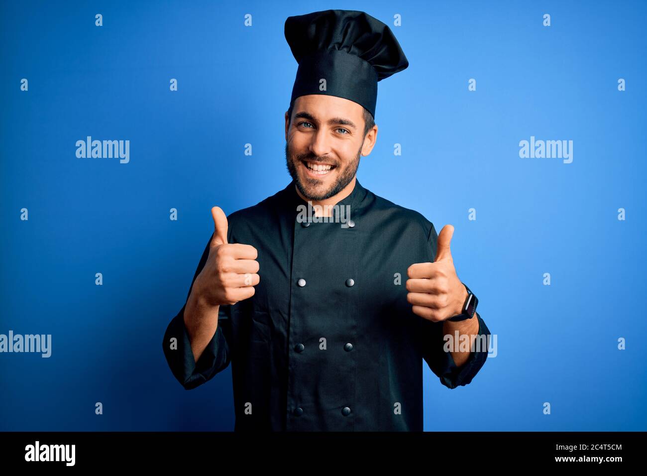 Young handsome chef man with beard wearing cooker uniform and hat over ...