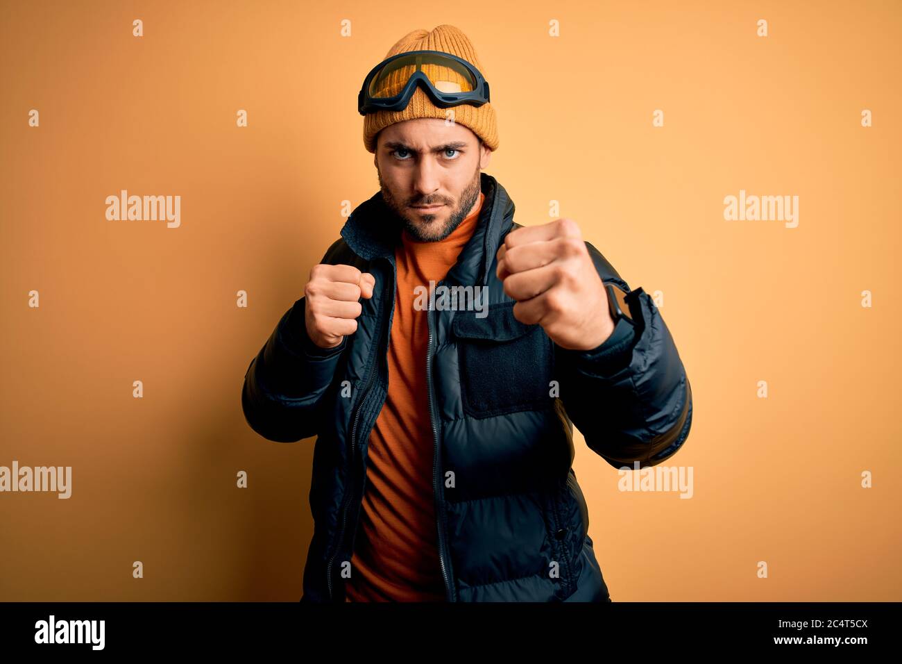 Young handsome skier man with beard wearing snow sportswear and ski ...