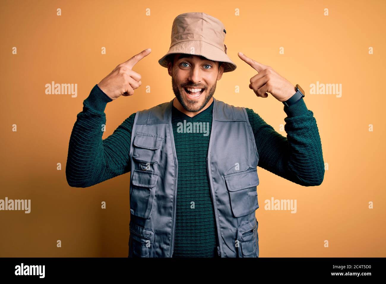 Handsome tourist man with beard on vacation wearing explorer hat over ...