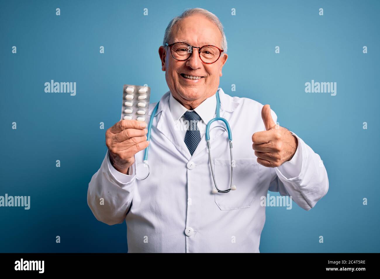 Senior grey haired doctor man holding pharmaceutical pills over blue ...