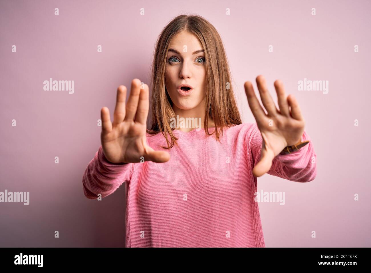 Young beautiful redhead woman wearing casual sweater over isolated pink ...