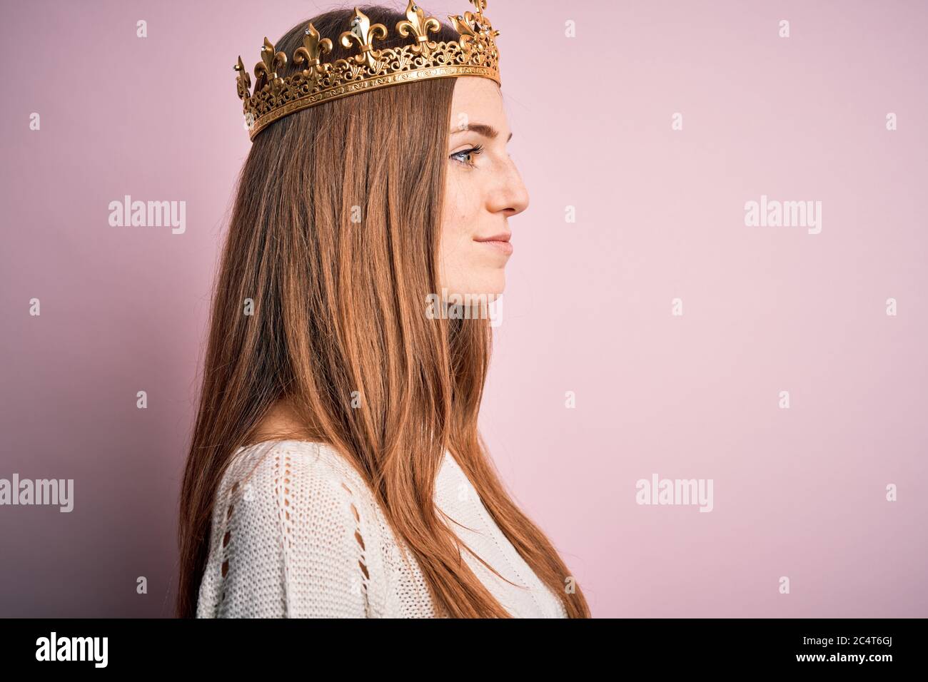 Young beautiful redhead woman wearing queen crown over isolated pink ...