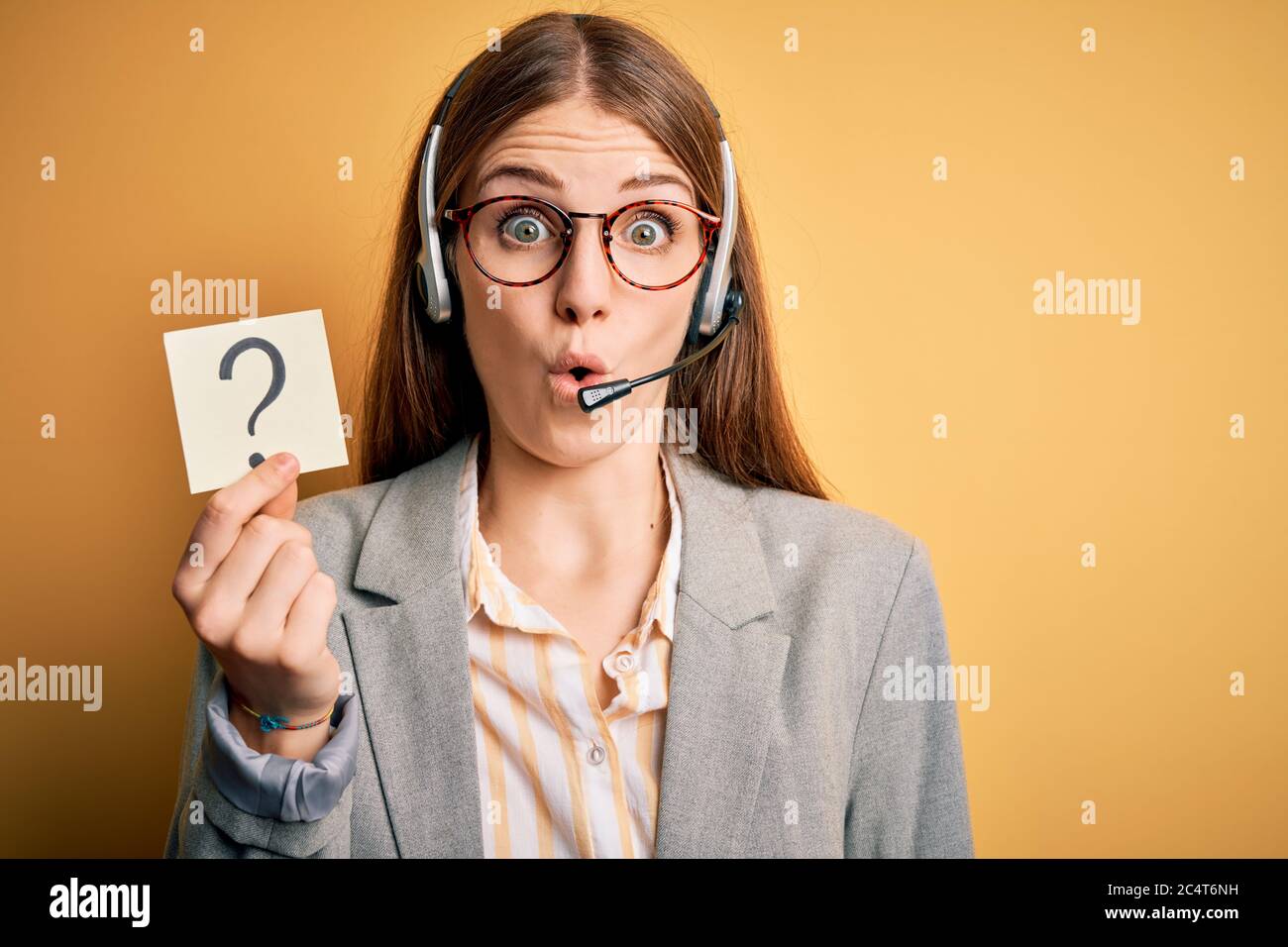 Young redhead call center agent woman using headset holding question ...