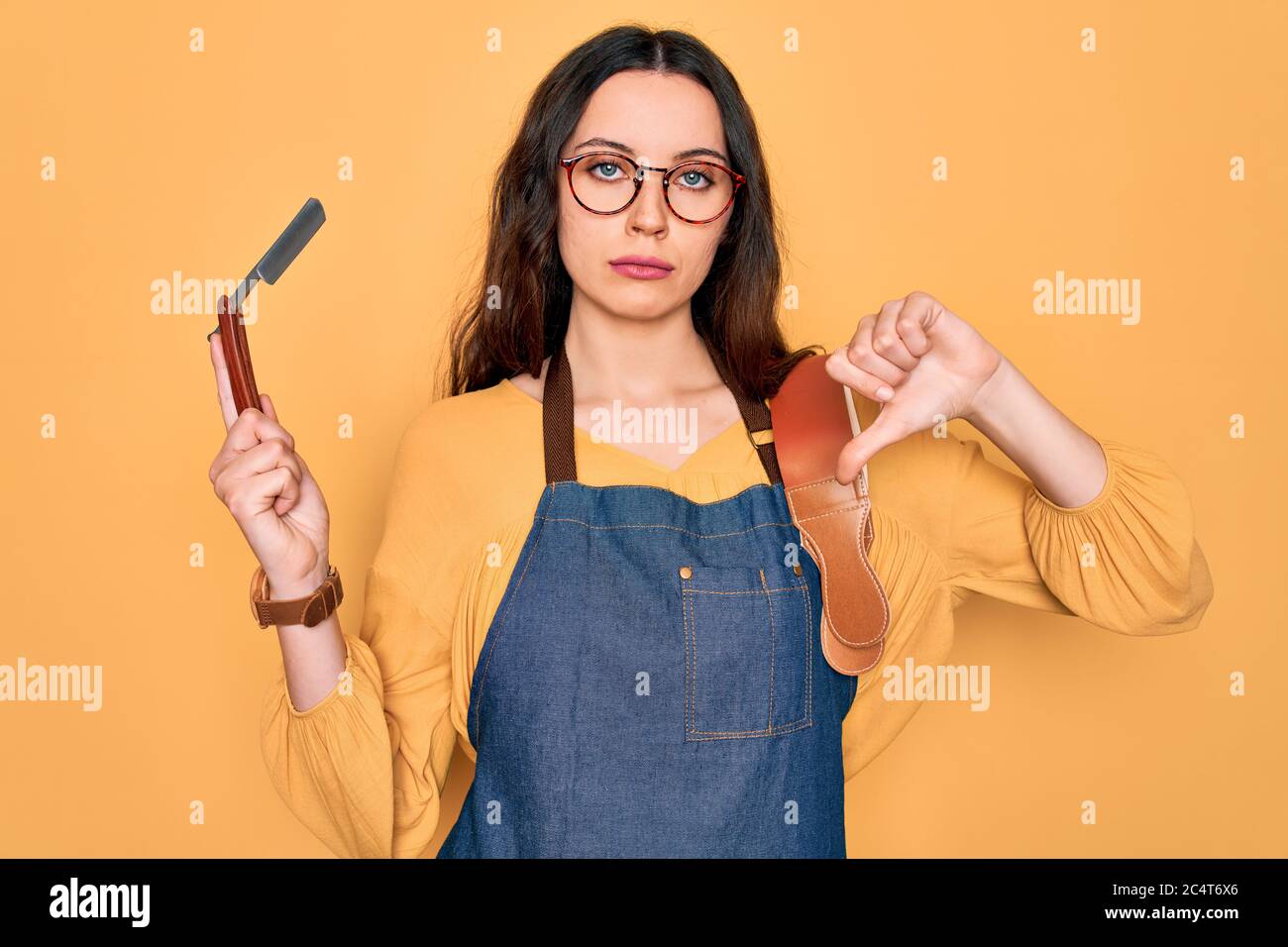 Young beautiful barber woman wearing apron holding razor blade over ...