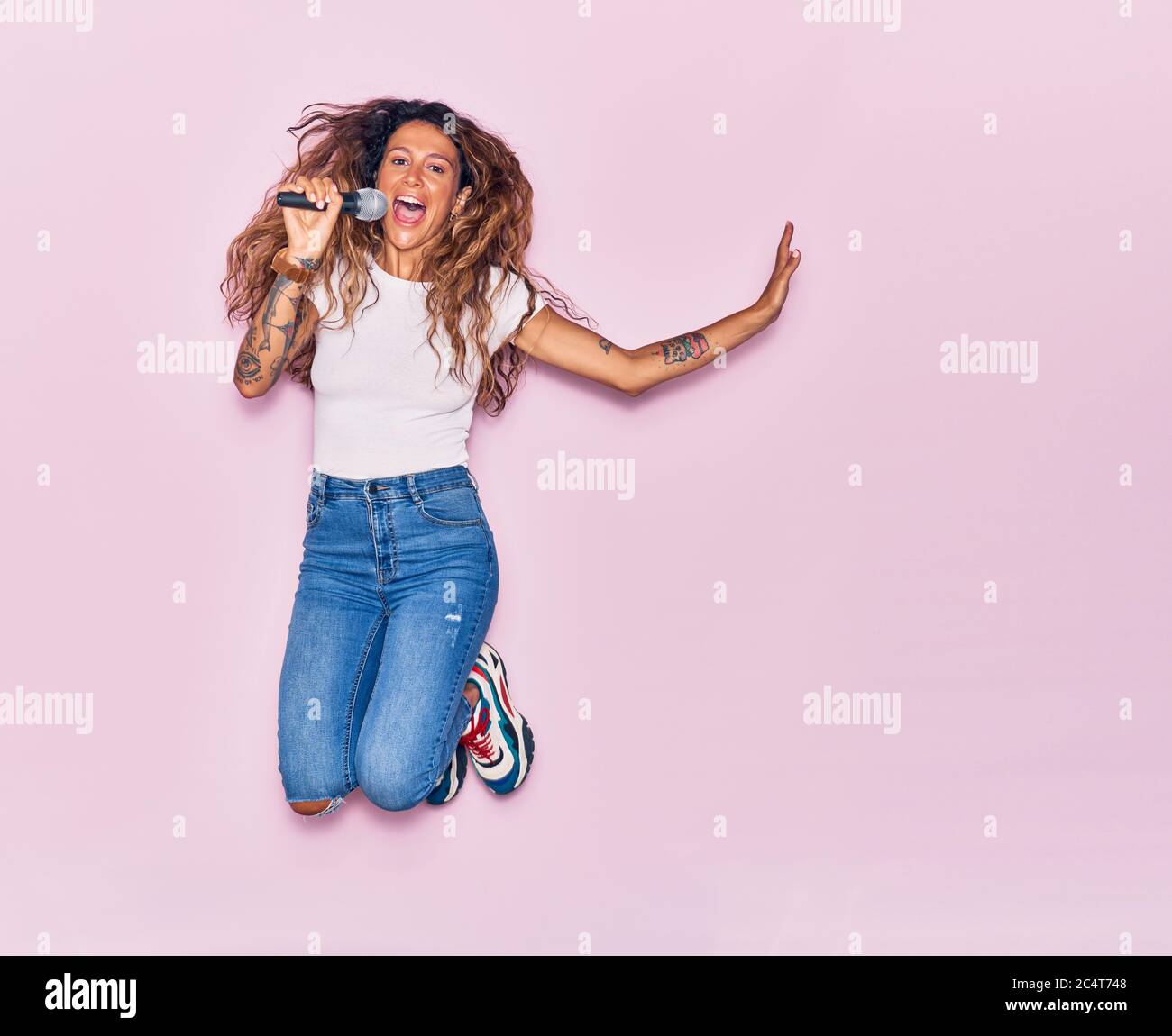 Young beautiful curly singer woman with tattoo smiling happy. Jumping ...