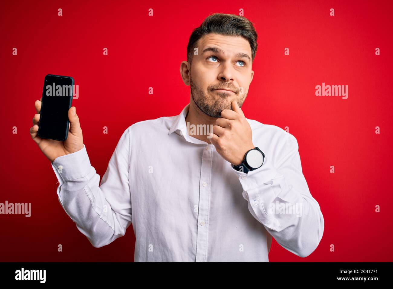 Young business man with blue eyes showing smartphone screen over red ...