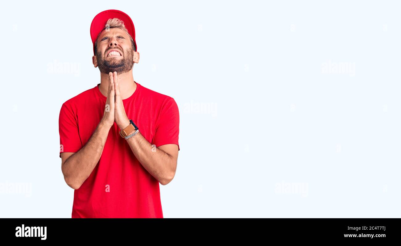 Young handsome blond man wearing t-shirt and cap begging and praying ...