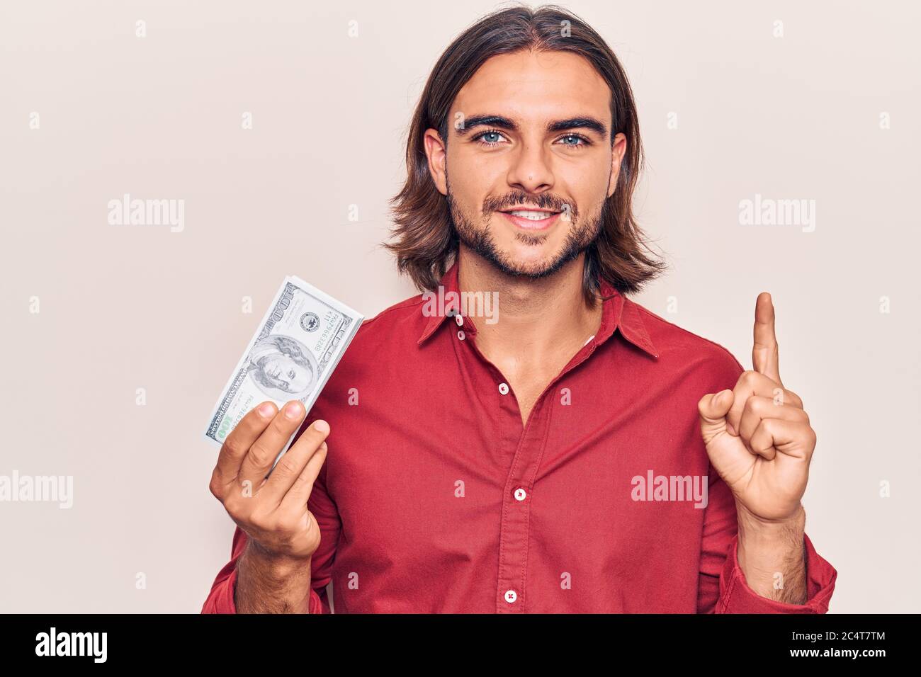 Young handsome man holding dollars smiling with an idea or question ...