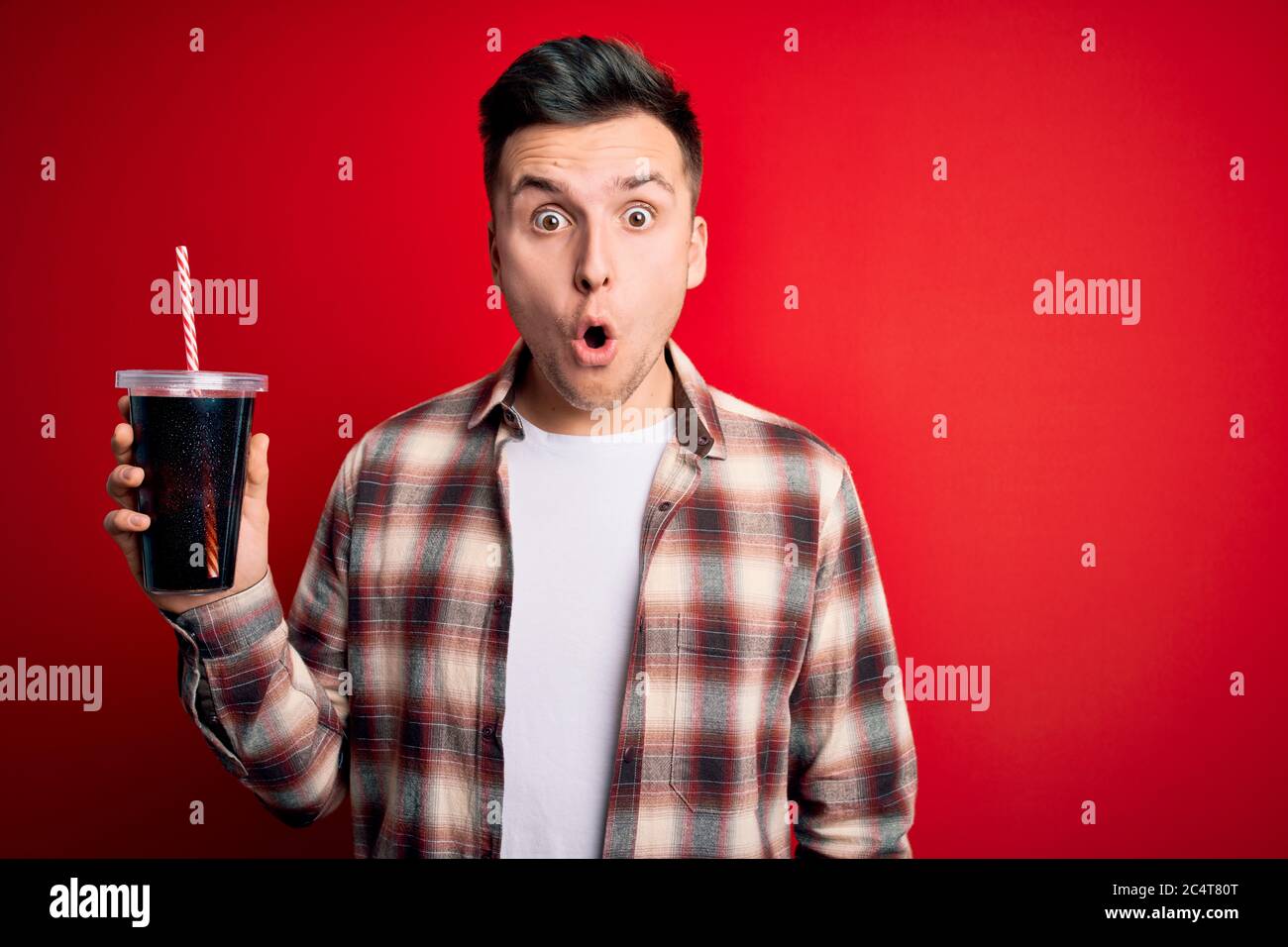 Young handsome caucasian man drinking a fresh soda refreshment over red ...
