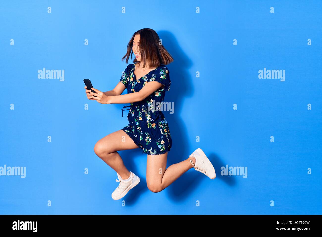 Young beautiful chinese woman jumping with smile on face. Make selfie ...