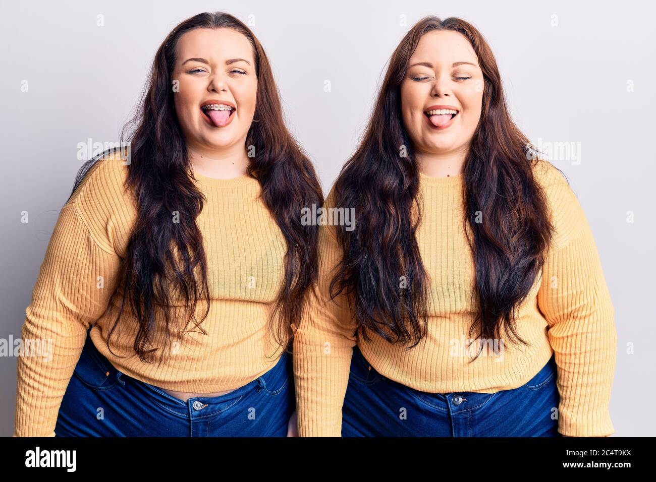 Young plus size twins wearing casual clothes sticking tongue out happy ...