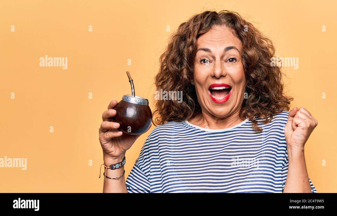 Middle age beautiful woman drinking cup of mate over isolated yellow ...