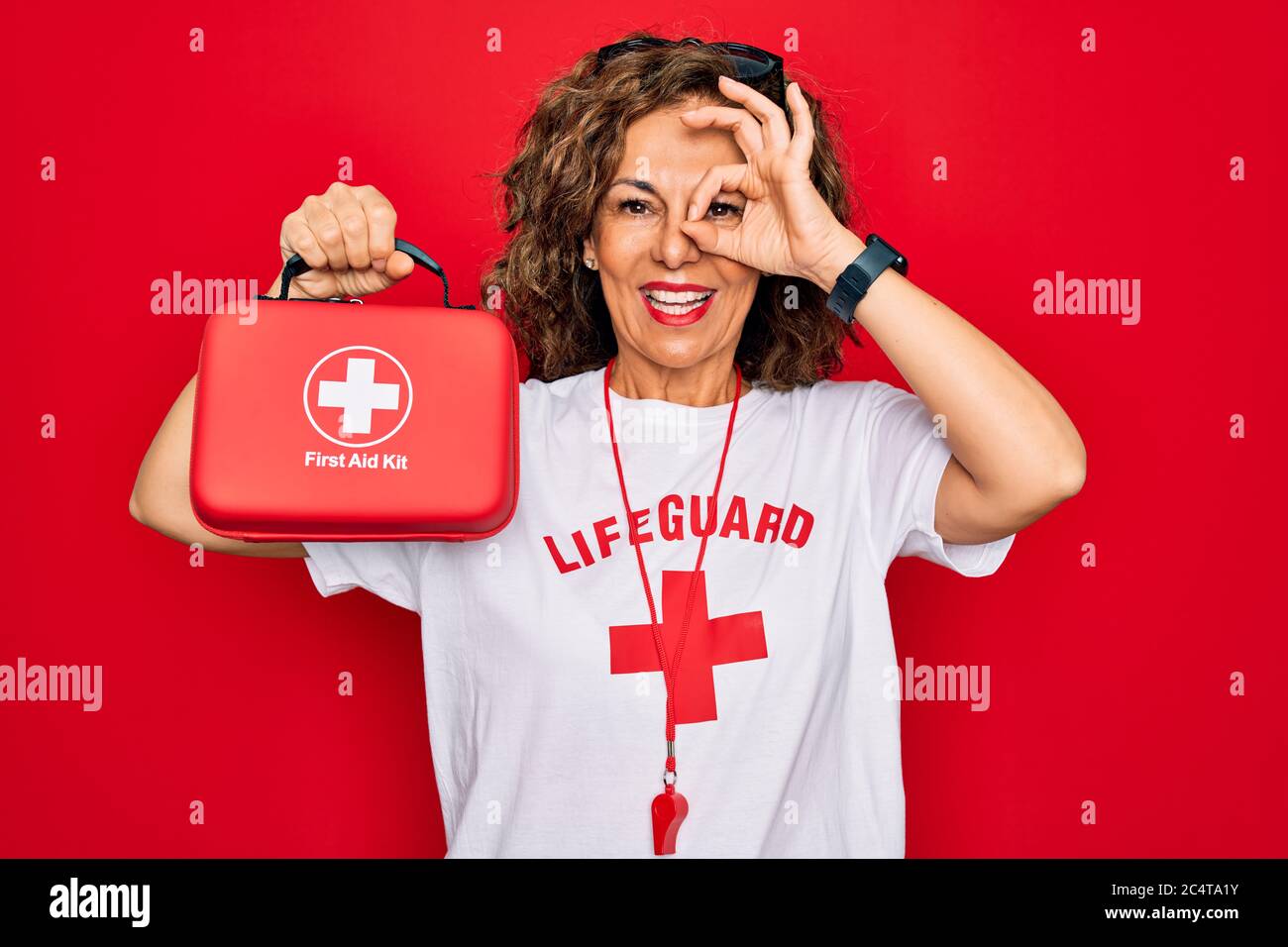 Middle age senior summer lifeguard woman holding first aid kit over red ...