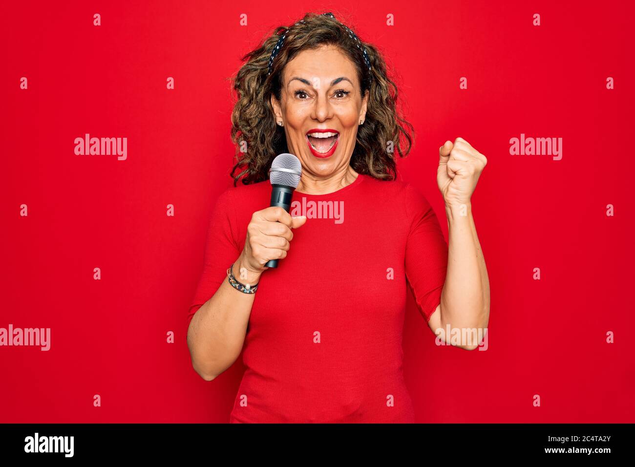 Middle age senior singer woman singing using music microphone over red ...