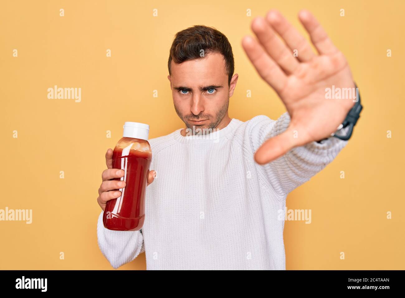 Young handsome man holding bottle of ketchup sauce condiment over ...