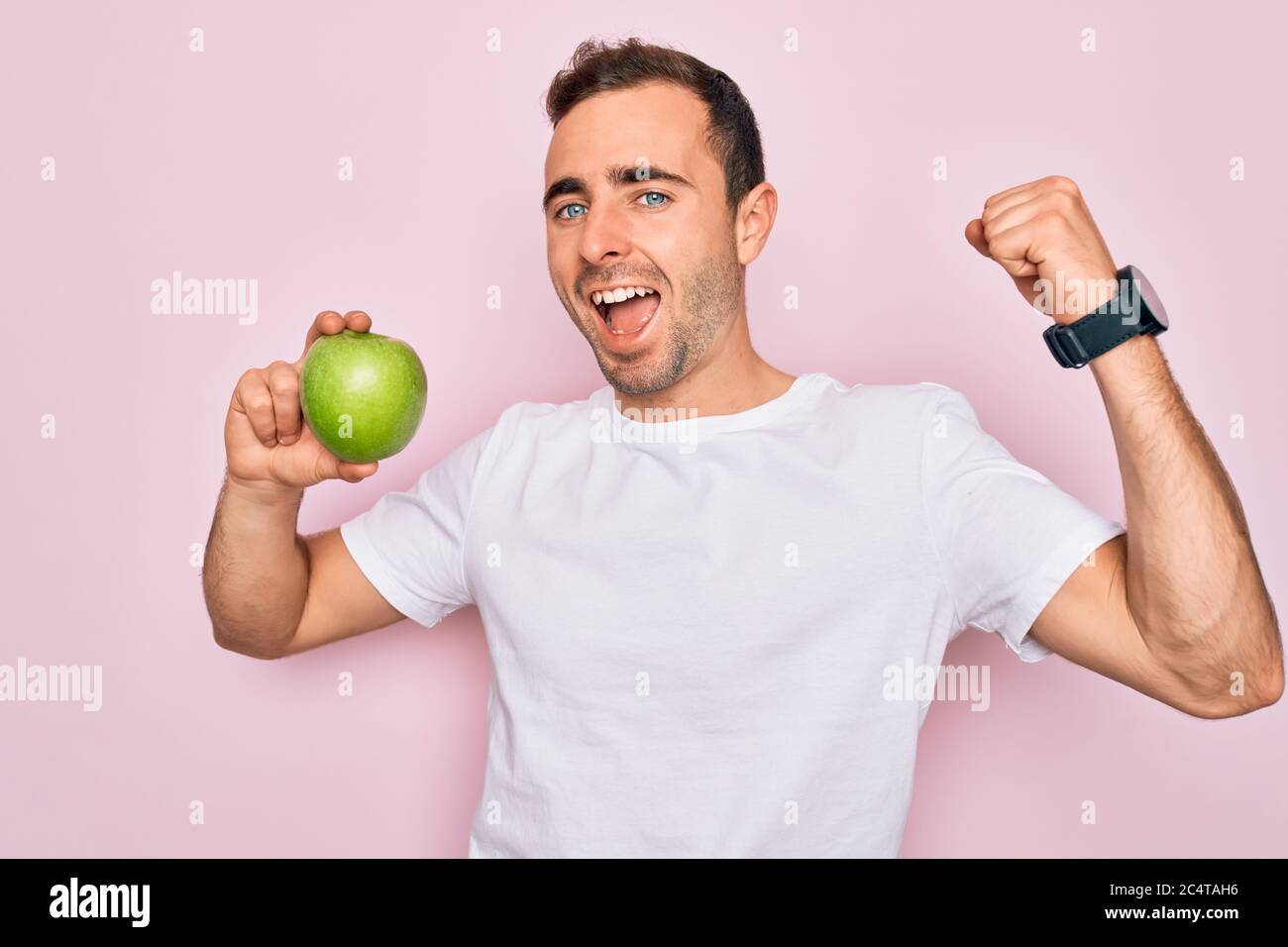 Young handsome man with blue eyes eating healthy green apple over ...