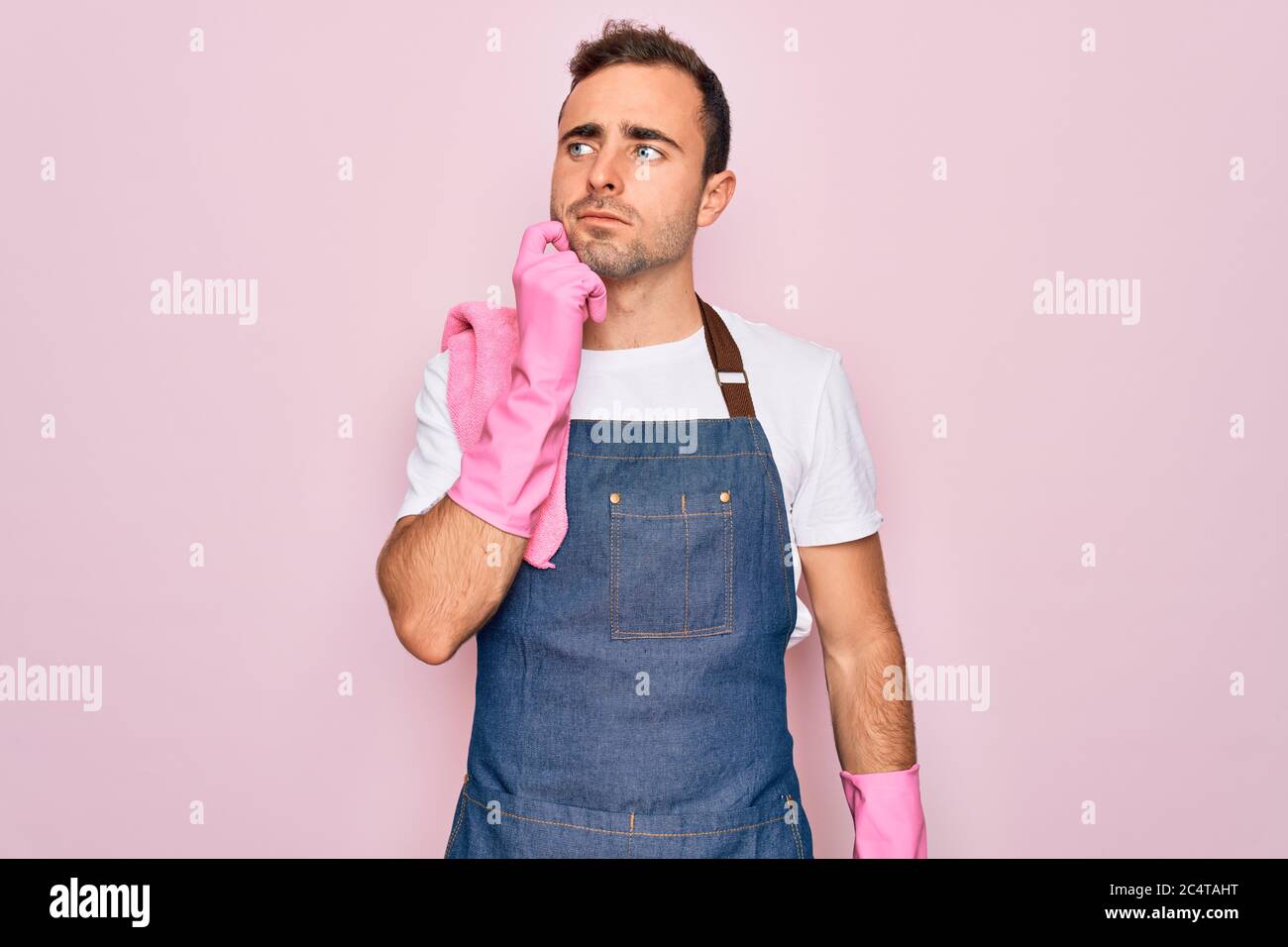 Young cleaner man with blue eyes cleaning wearing apron and gloves over ...