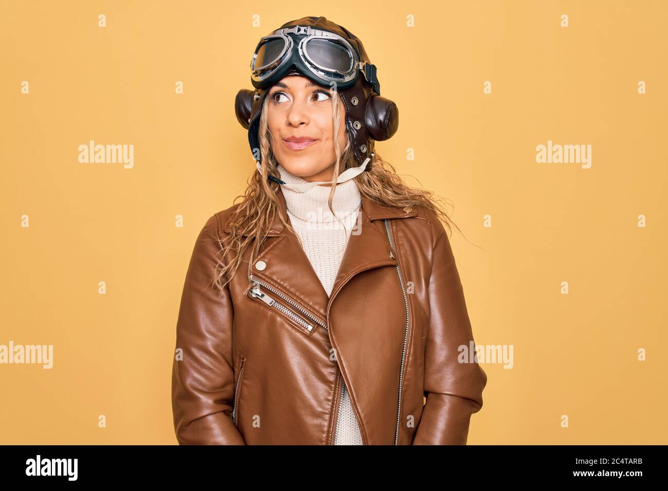 Young beautiful blonde aviator woman wearing vintage pilot helmet whit ...