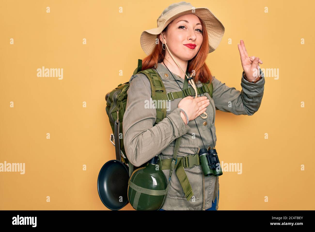Young redhead backpacker woman hiking wearing backpack and hat over ...