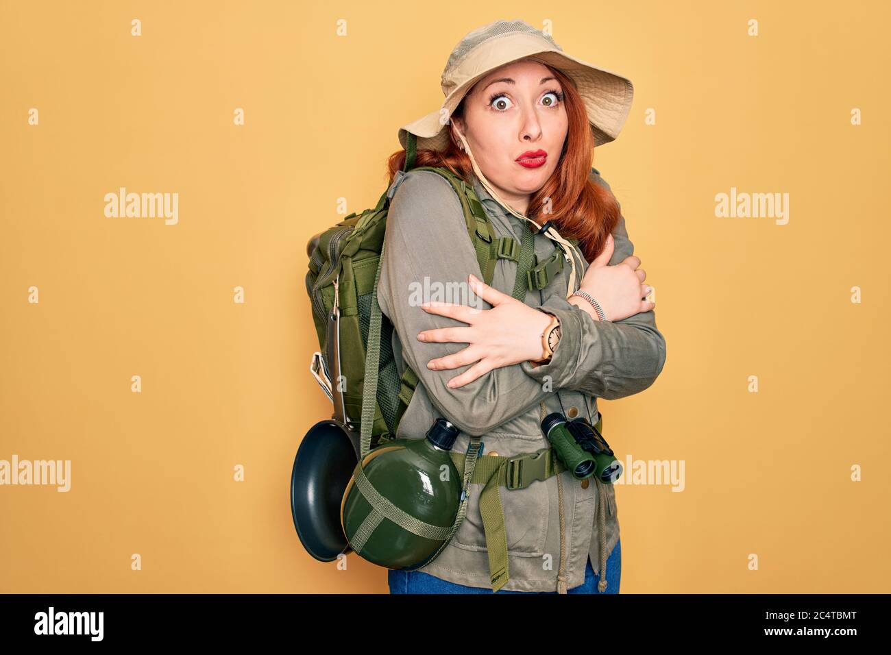 Young redhead backpacker woman hiking wearing backpack and hat over ...