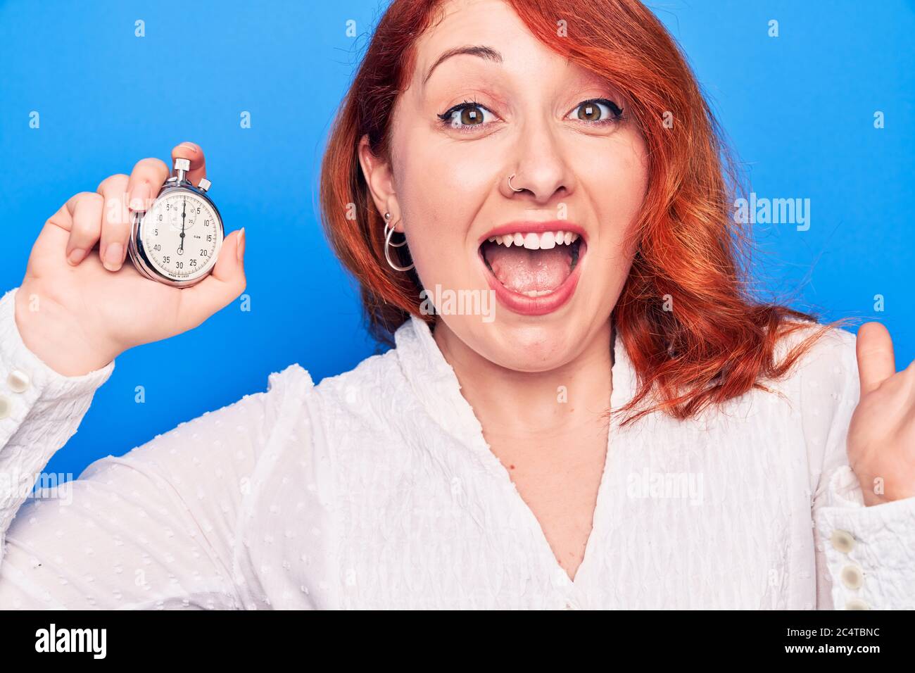 Young beautiful redhead woman doing countdown using stopwatch over blue ...