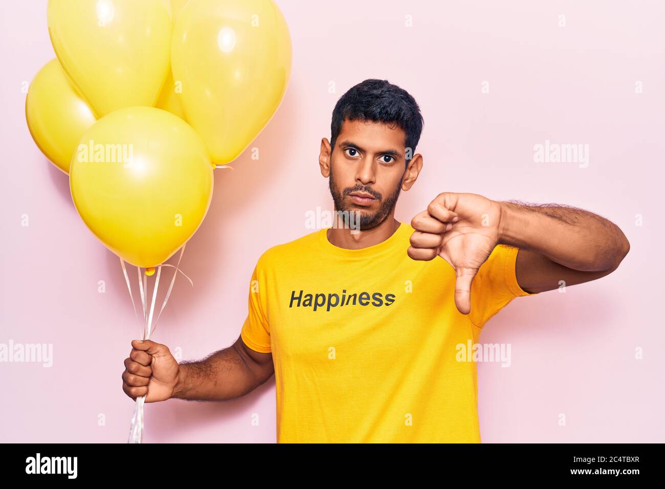 Young latin man wearing t shirt with happiness message holding balloons ...