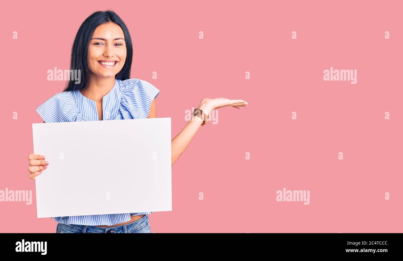 Young beautiful latin girl holding blank empty banner celebrating ...