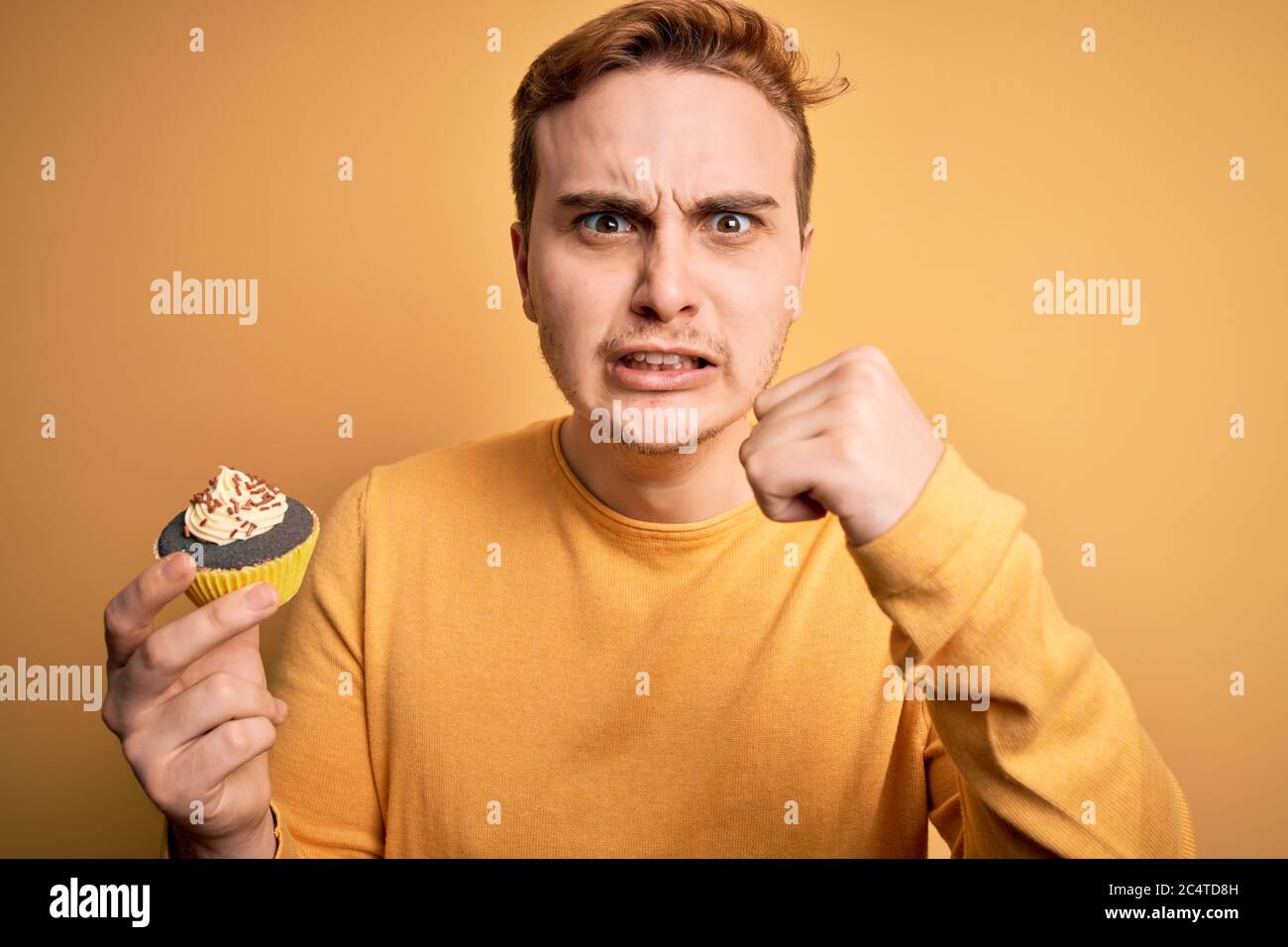 Young handsome redhead man eating sweet chocolate cupcake dessert over ...