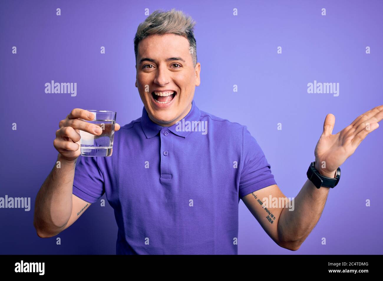 Young modern man drinking a glass of fresh water over purple isolated ...