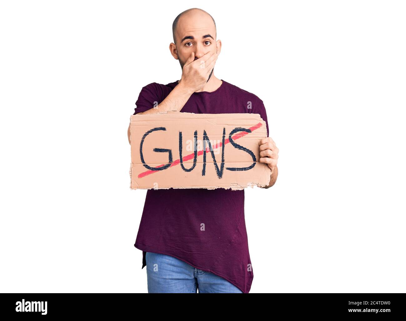 Young handsome man holding prohibited guns banner covering mouth with ...