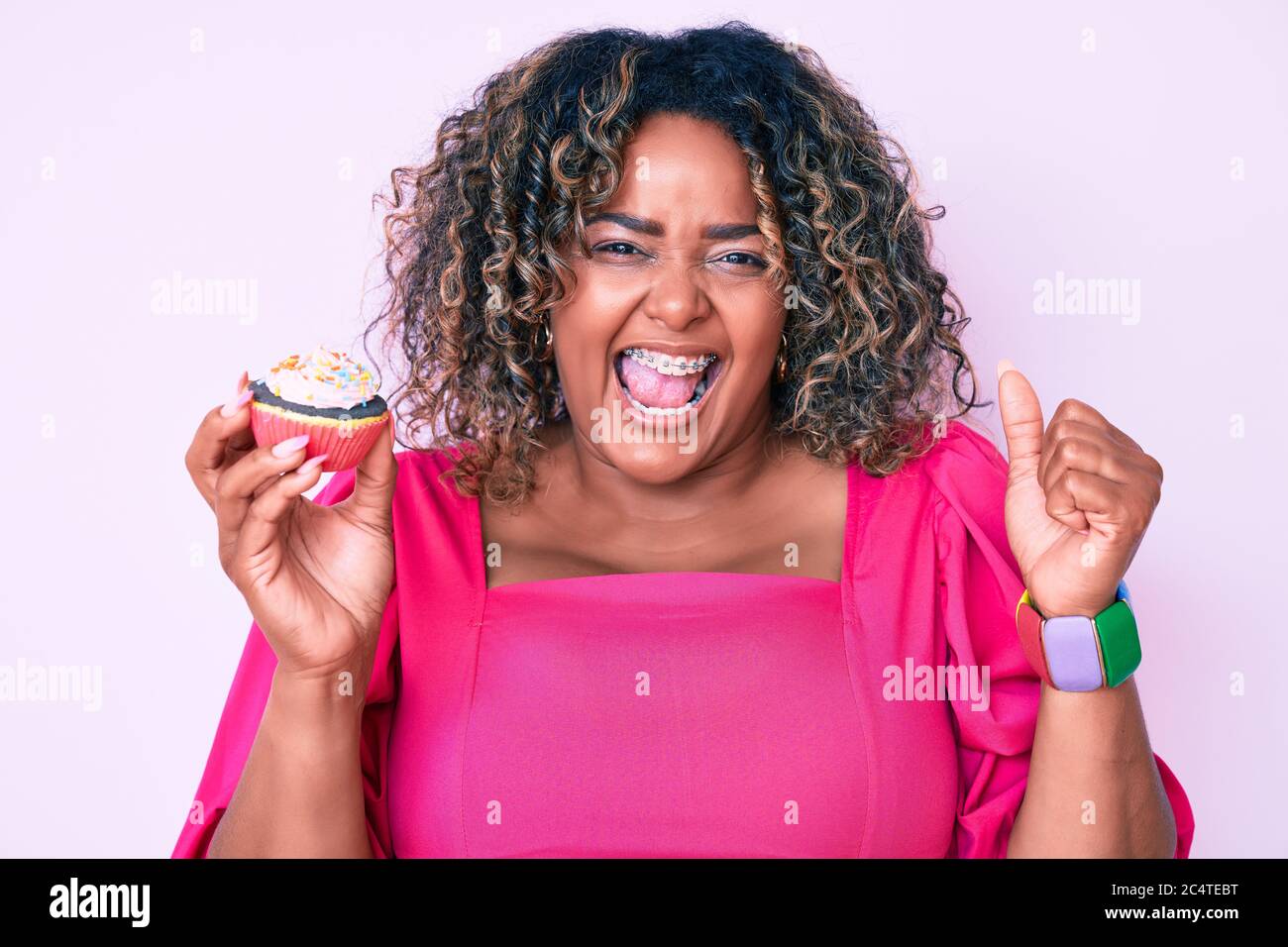 Young african american plus size woman holding cupcake screaming proud ...