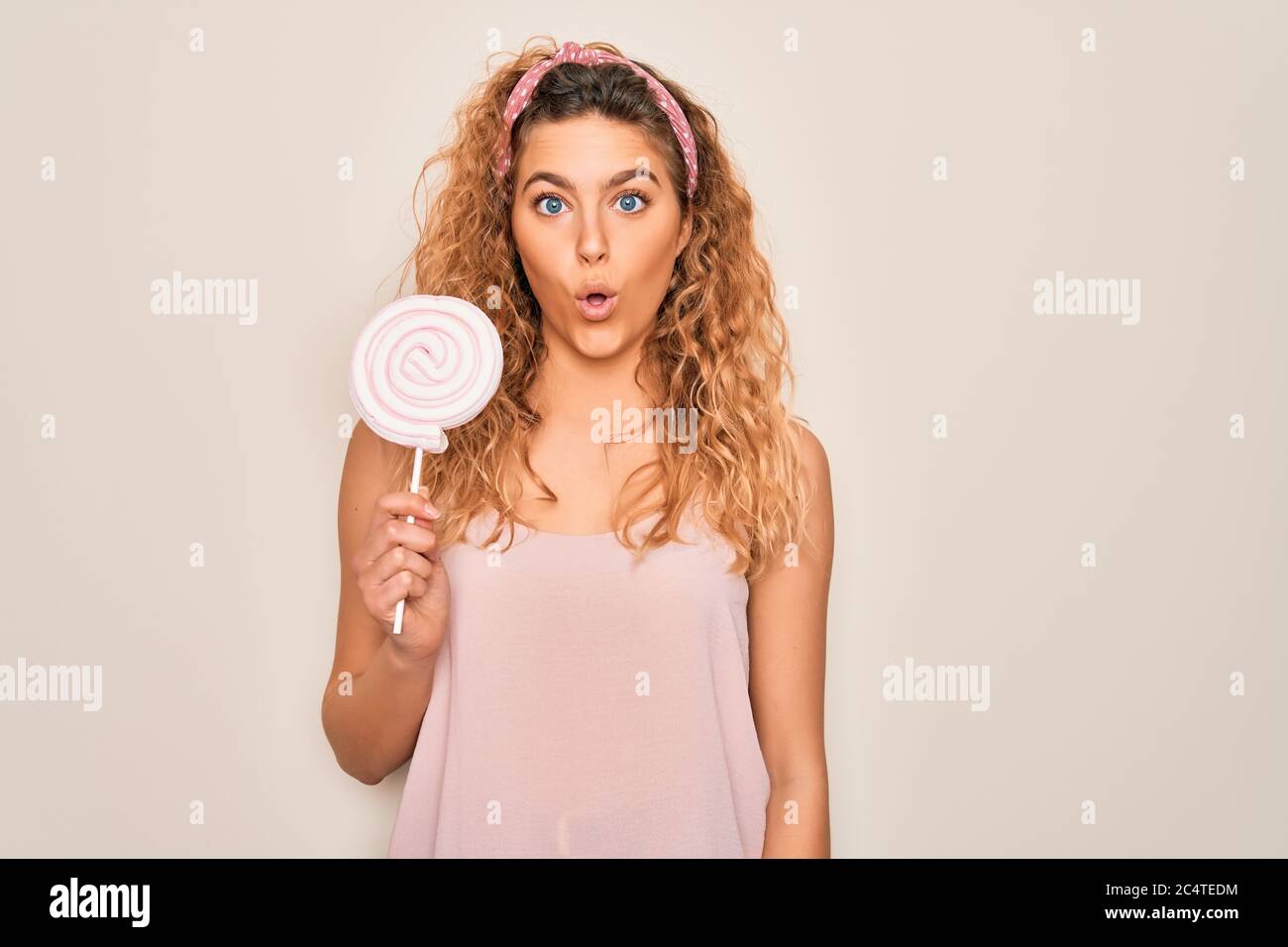 Young beautiful blonde woman with blue eyes eating sweet candy lollipop ...
