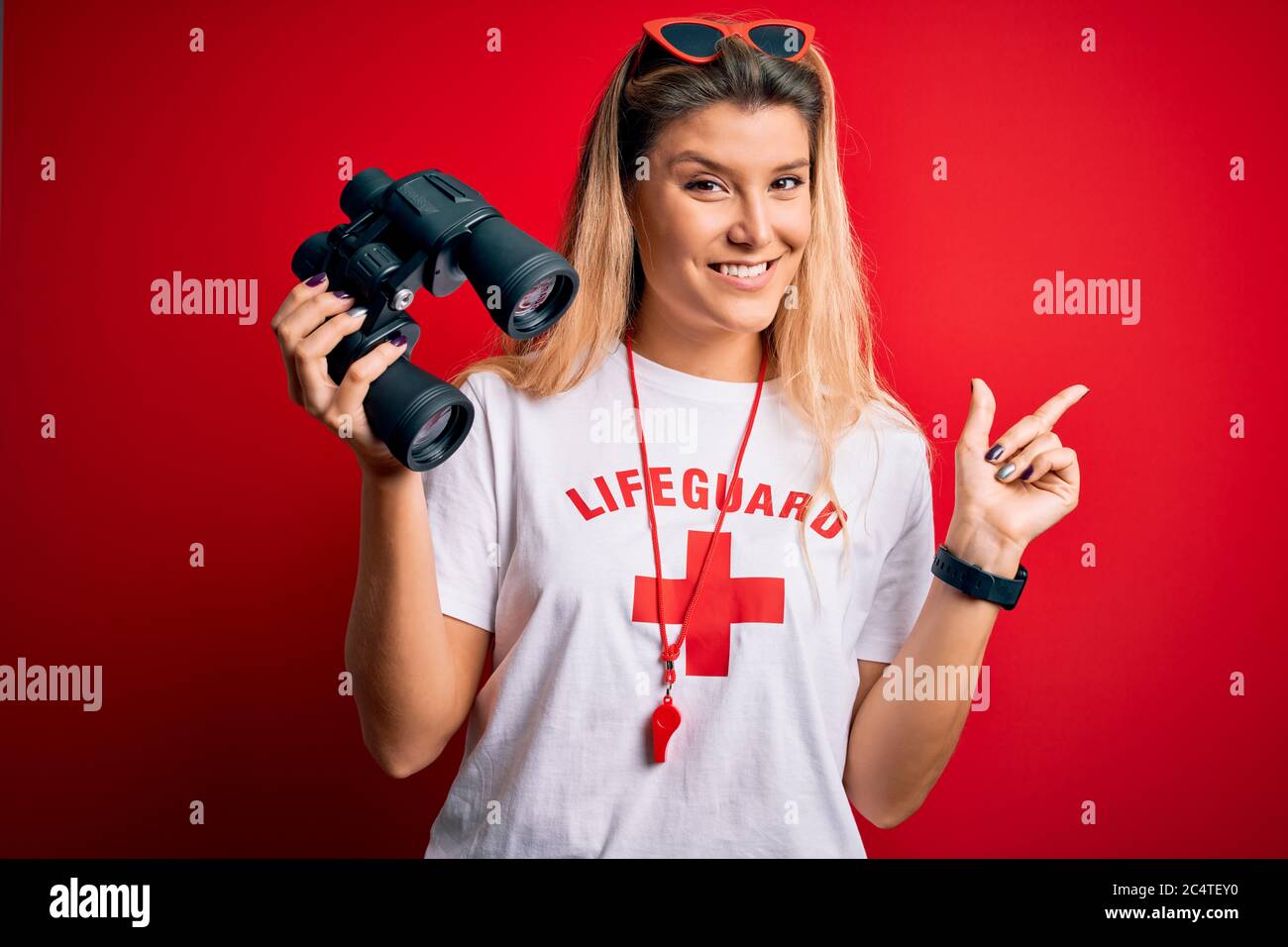 Young beautiful blonde lifeguard woman using binoculars and whistle ...