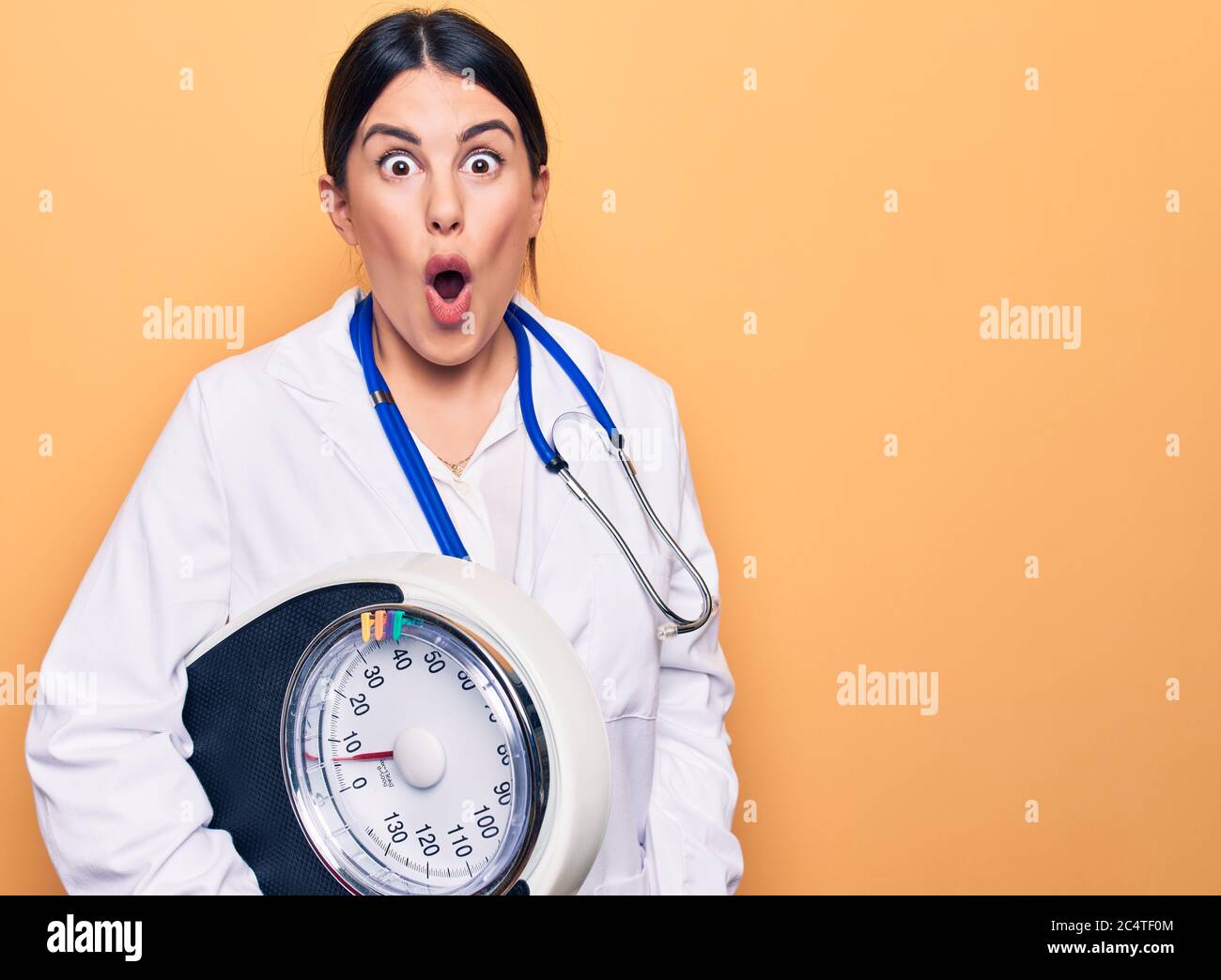 Young beautiful doctor woman wearing stethoscope and coat holding ...