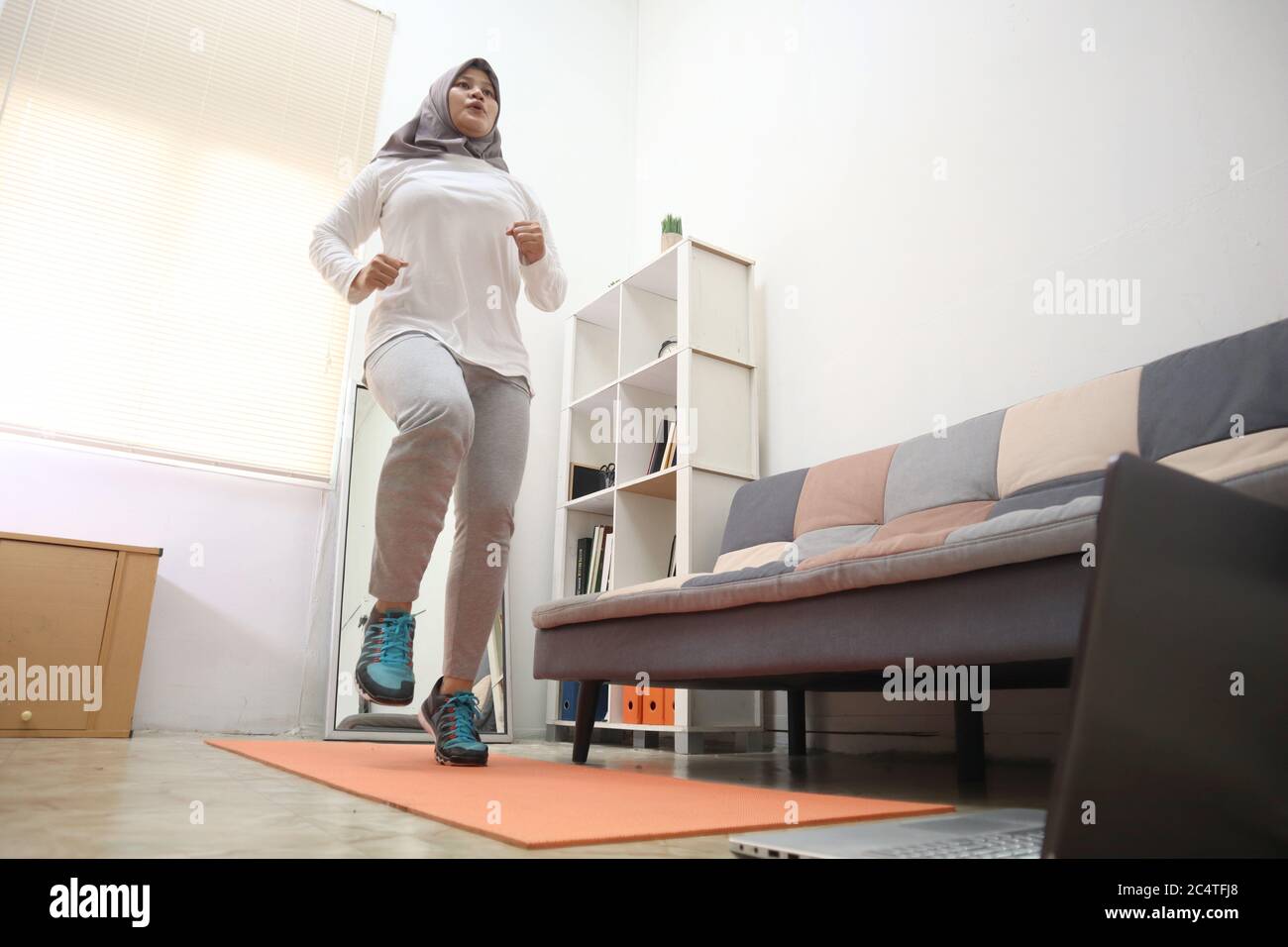 Asian muslim woman wearing hijab doing exercise at home while watching ...