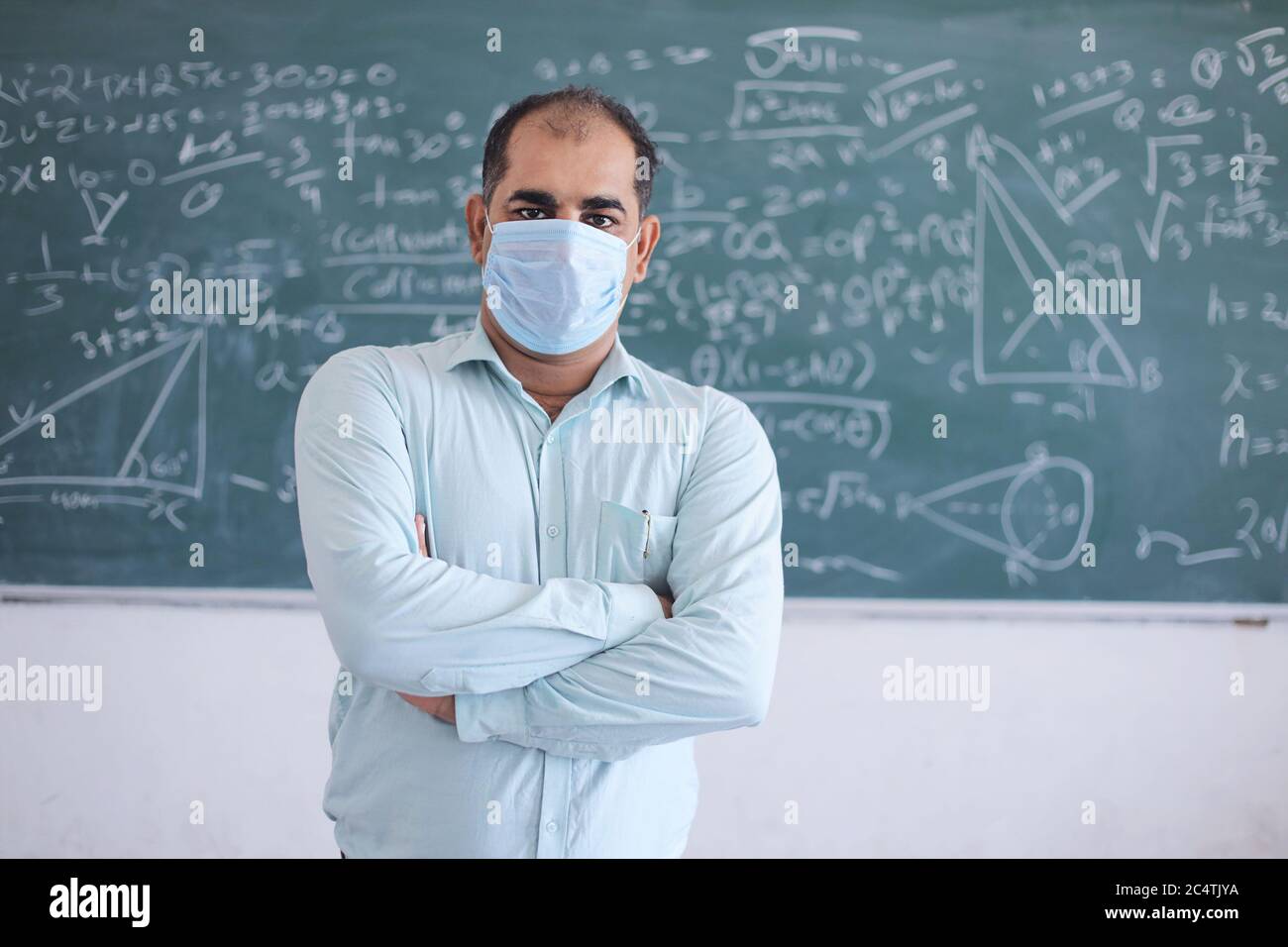 Portrait of male teacher wearing mask standing against blackboard ...