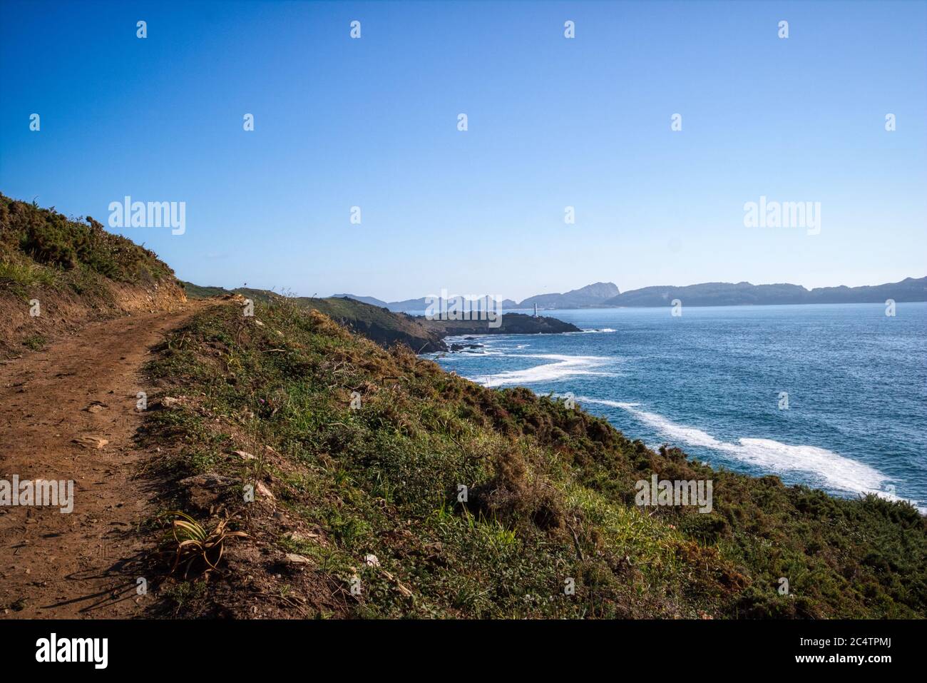Pathway leading to the wavy sea surrounded by hills under the blue sky ...