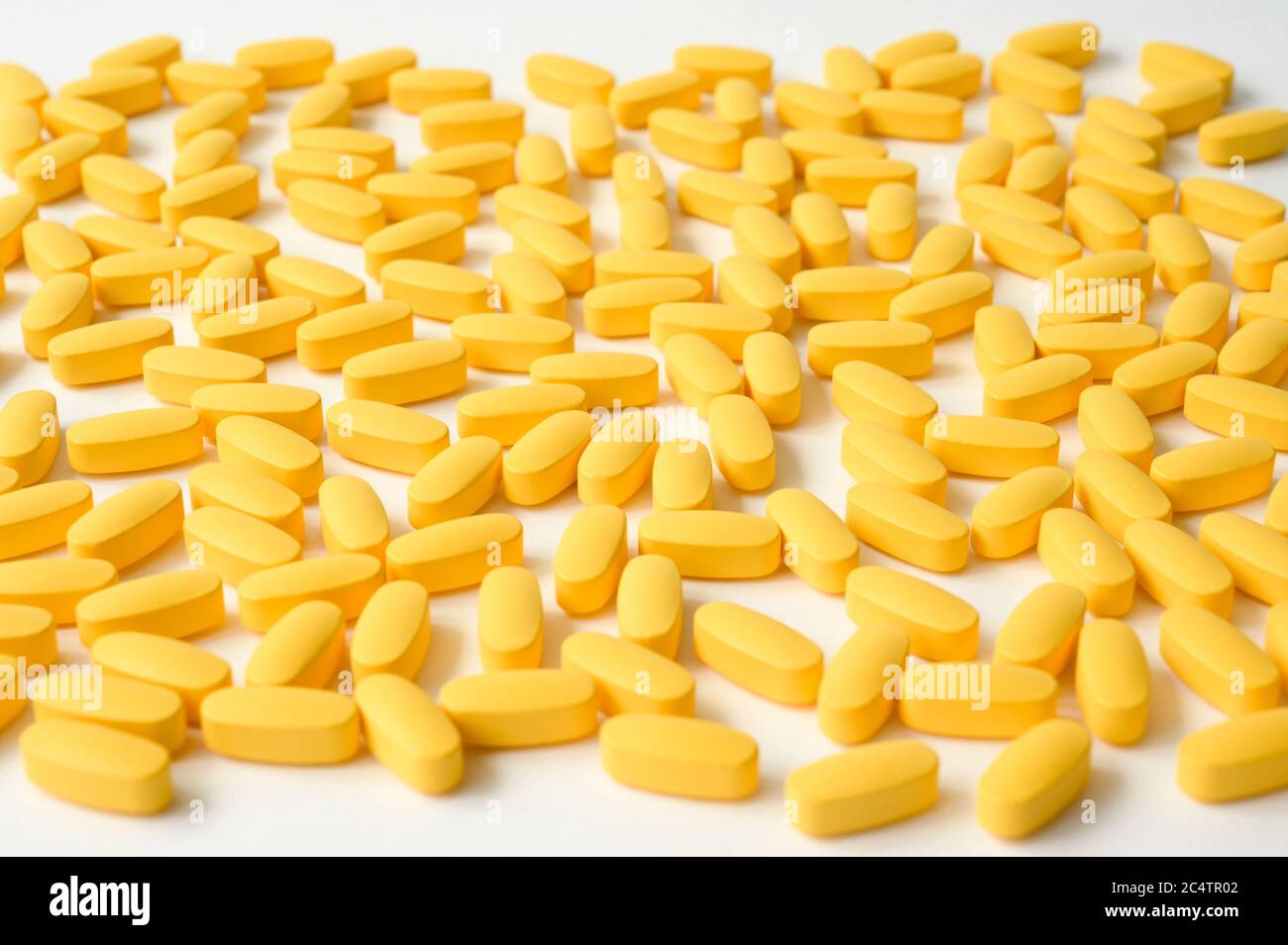 many yellow vitamin drug medication tablets lying on white surface ...