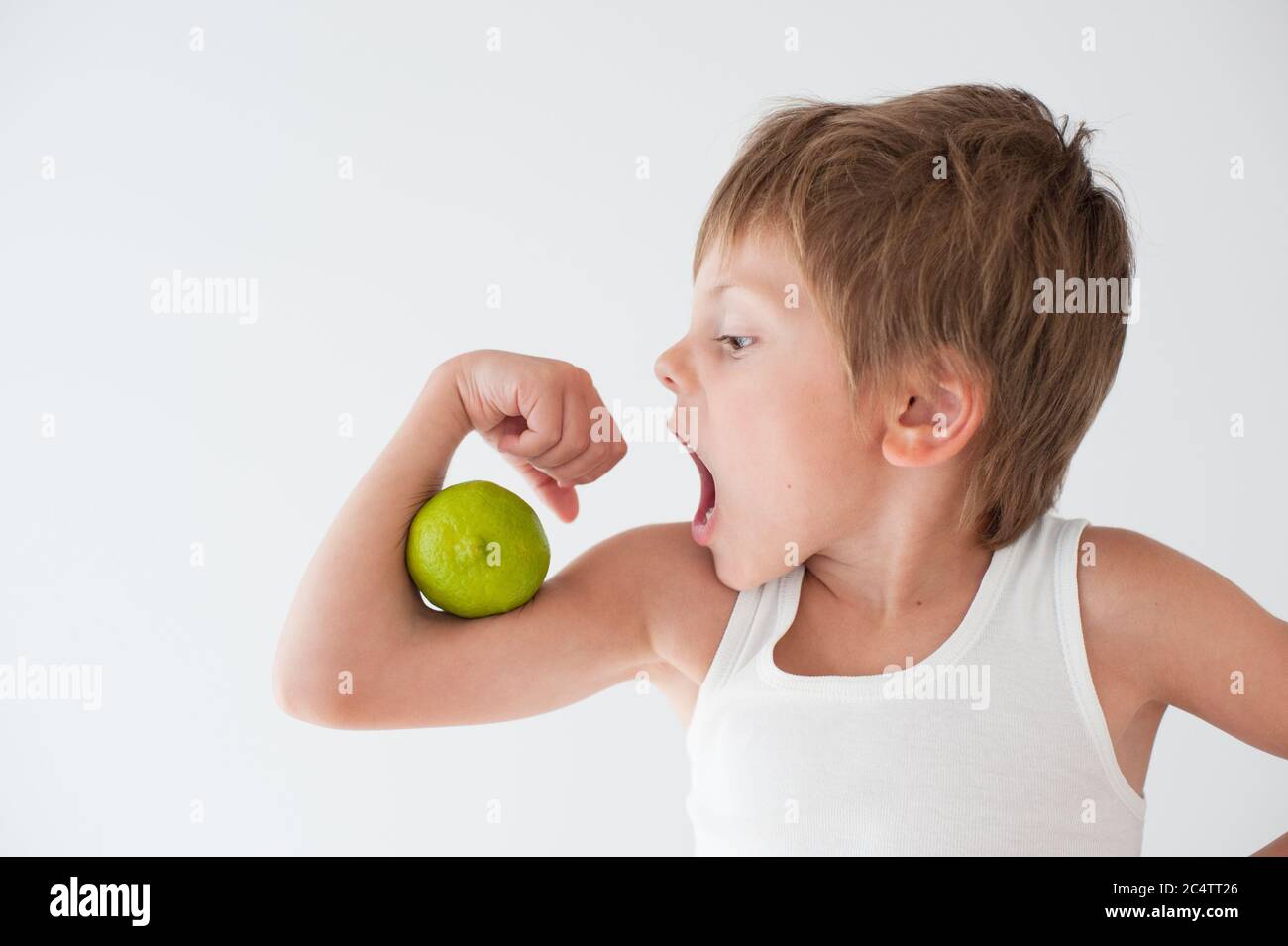 strong little child wants to eat green lime on his biceps muscle on ...