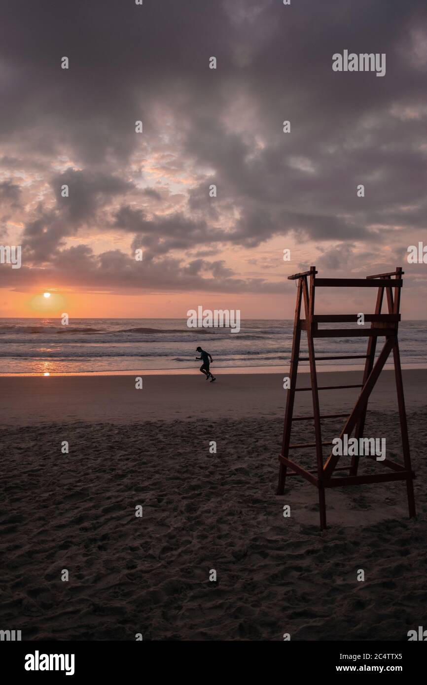 Lifeguard chair on sandy beach with setting sun in the horizon under a ...