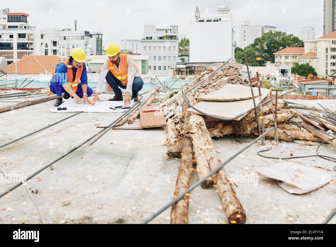 Construction workers checking blueprint on the ground next to pile of ...