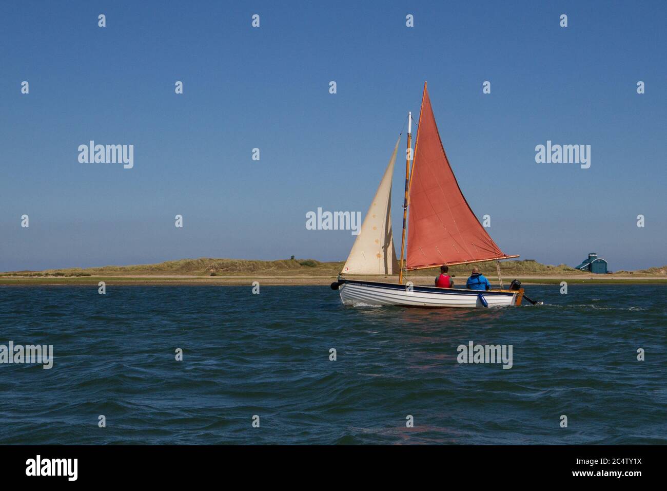 Eye-level shot of two people riding a sailboat with red and white sails ...