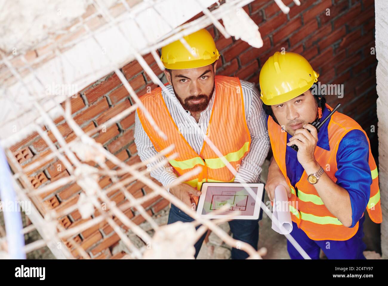 Builders working in building under construction, one holding tablet computer with blueprint, his ...
