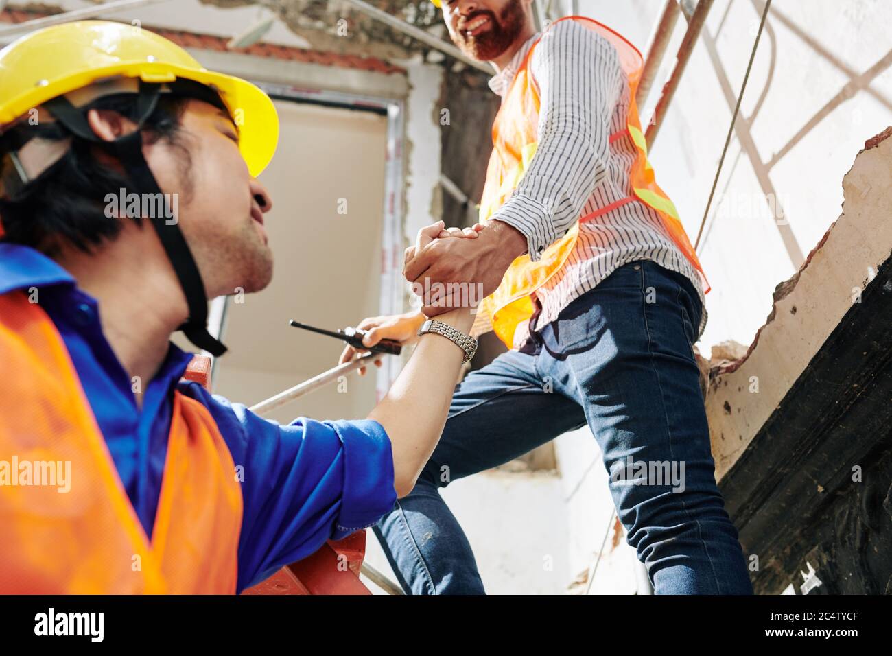 Smiling construction worker outstretching hand when helping colleague ...